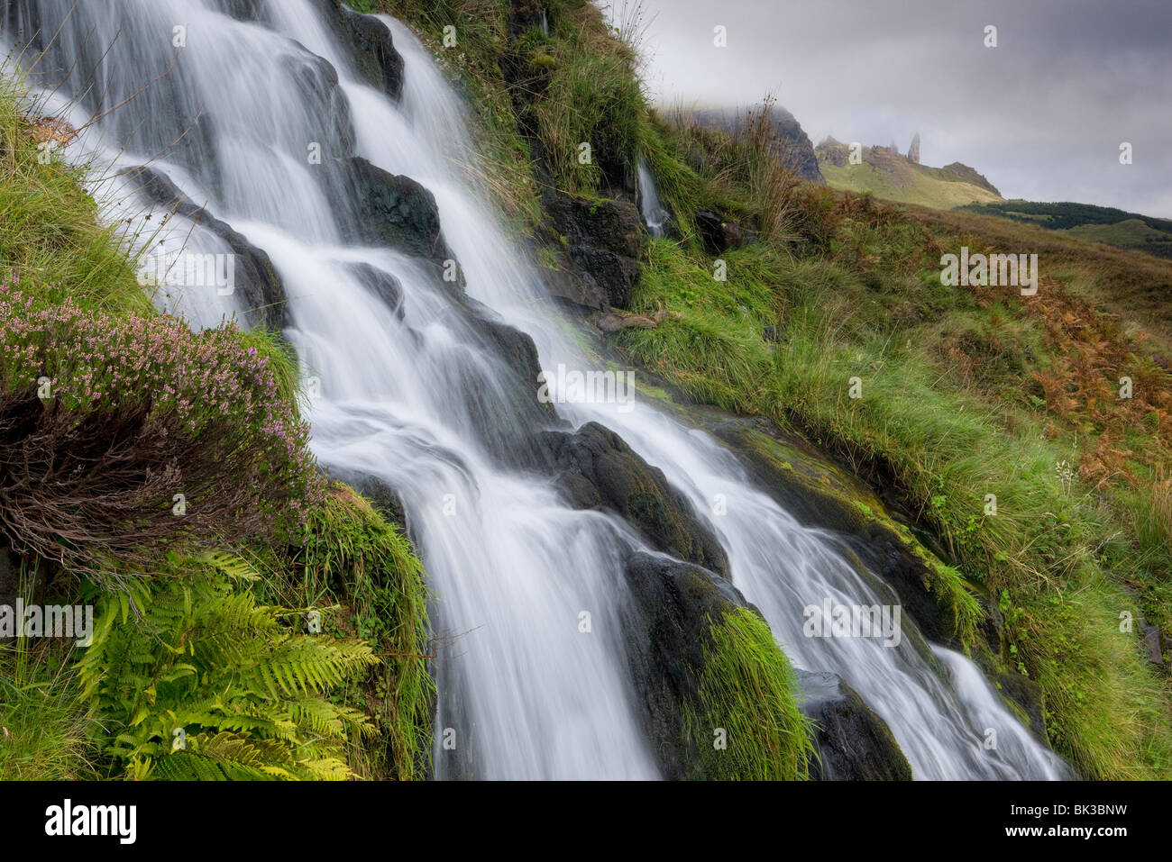 Waterfall cascading down grassy slope with Old Man of Storr in ...