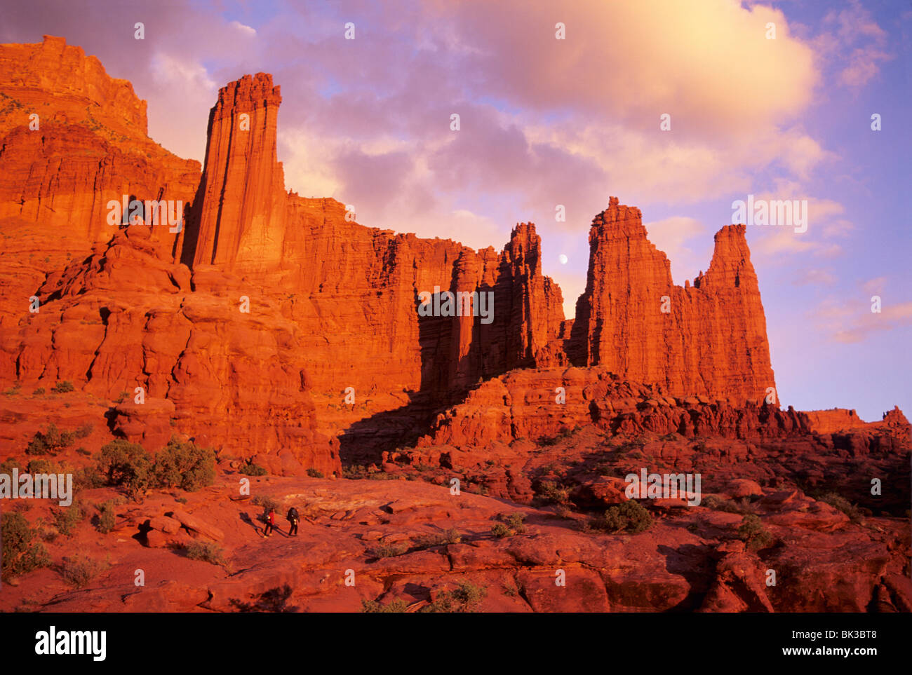 Two hikers approaching the Fisher Towers as the sun sets east of Moab ...