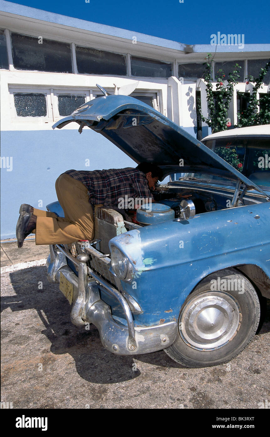 A car mechanic working under the hood in the engine compartment of a ...