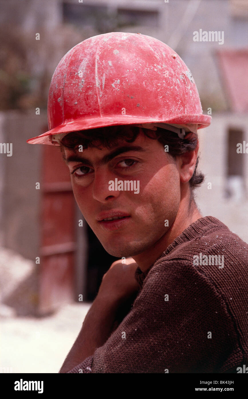 Portrait of a young construction worker wearing a red hardhat, Israel ...