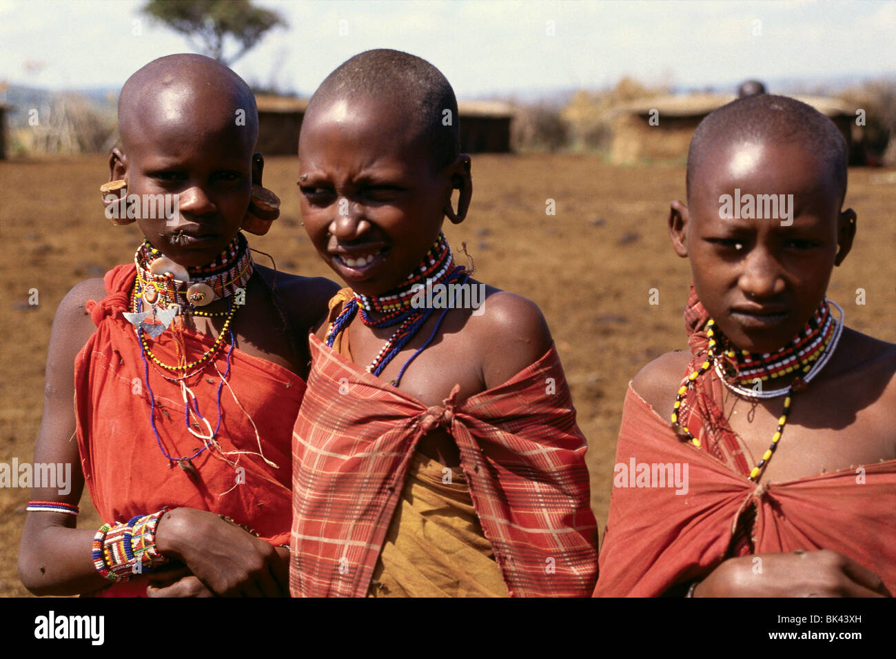 Three Maasai children wearing jewelry and one child is wearing wooden ...