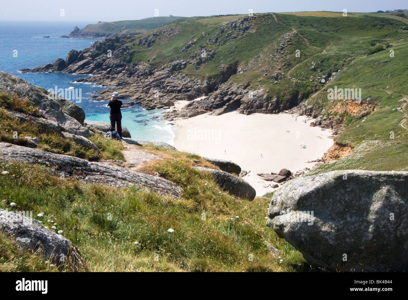 a man stands on the coastal footpath looking down on a secluded beach ...