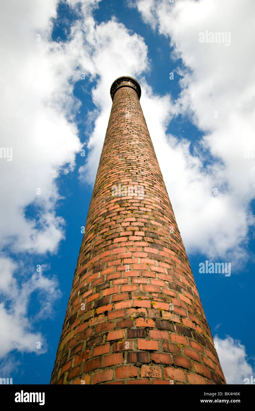 A tall brick chimney stack stretching up to a blue sky full of white ...