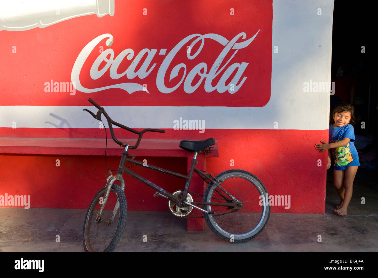 A young girl and a bicycle in front of a coca cola sign in rural mexico ...