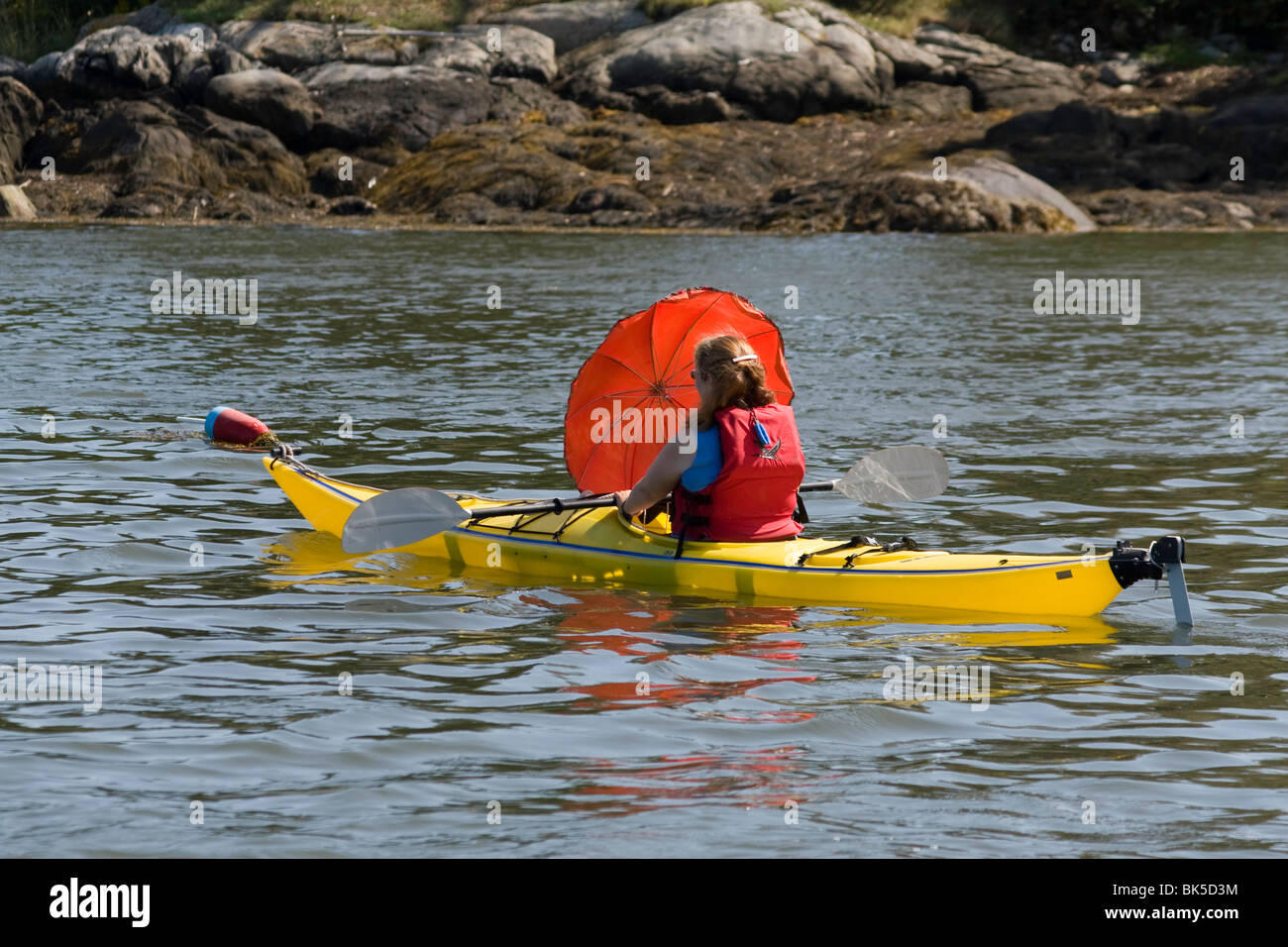 A woman in a yellow kayak employs an orange umbrella as a sail to slide ...
