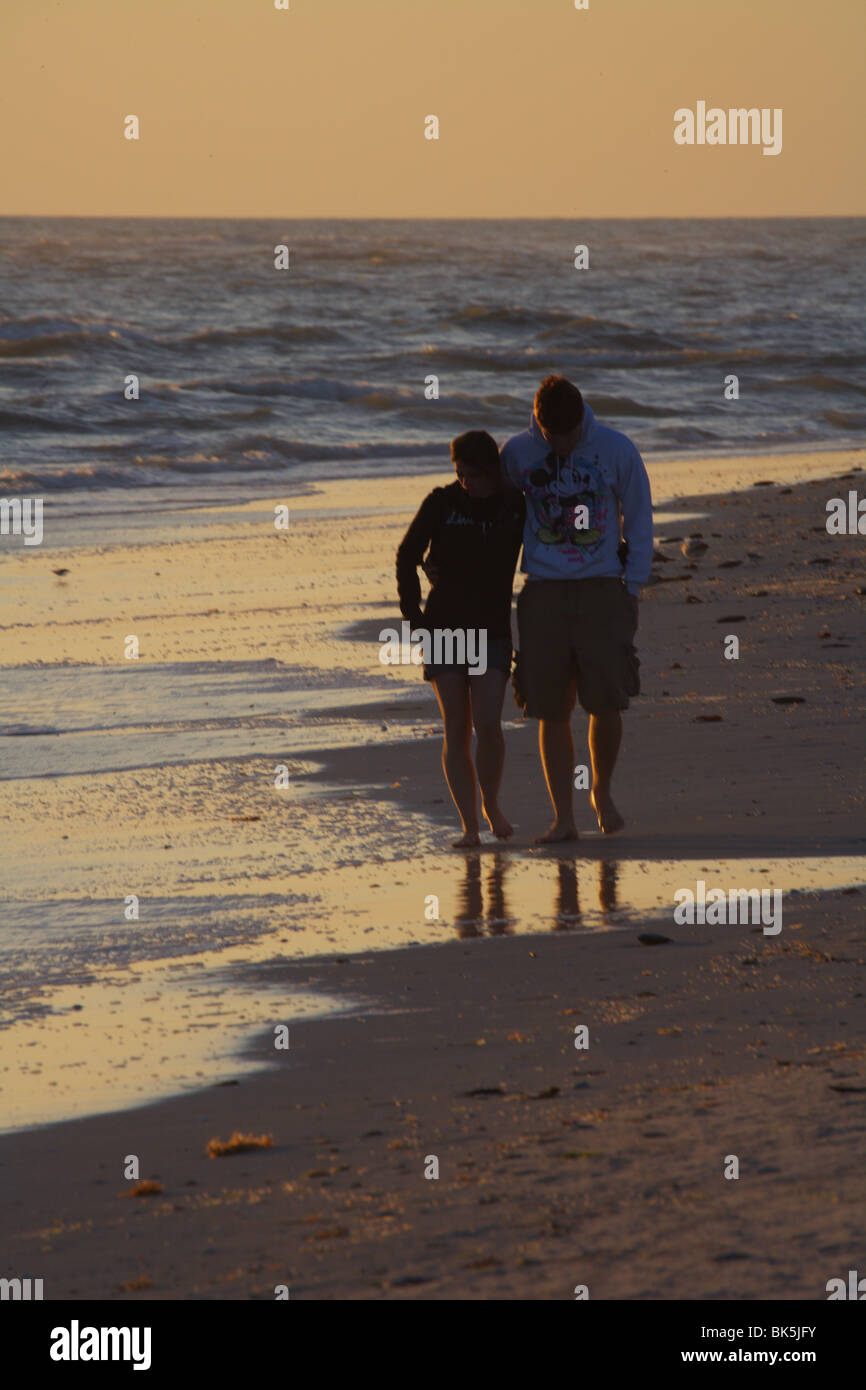 YOUNG MAN AND WOMAN WALKING ON BEACH IN FRONT OF OCEAN WAVES SUNSET ...