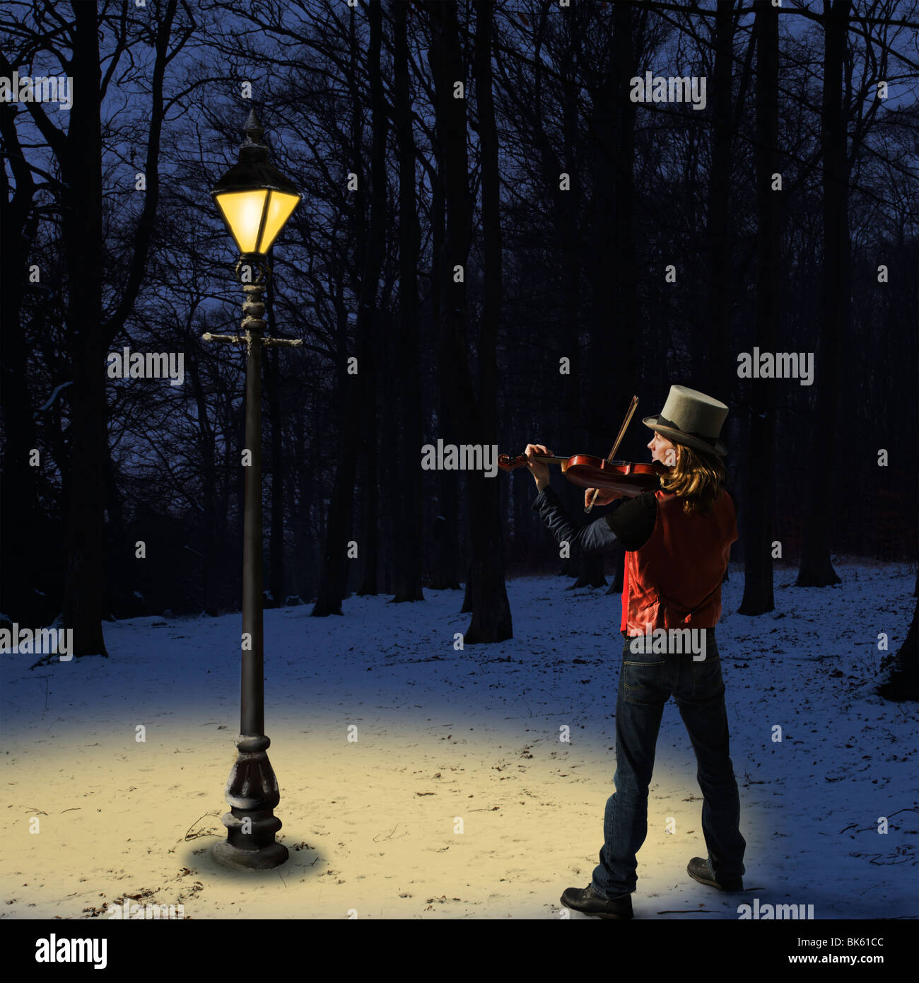 A musician plays a violin by gaslight in a snow covered woodland Stock ...