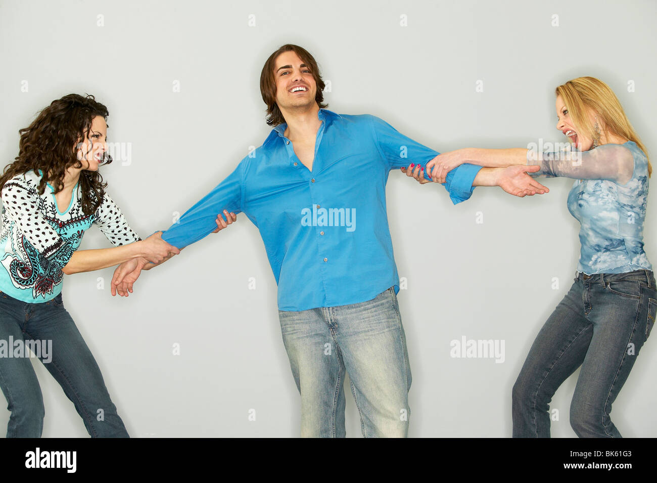 Two young women pulling the arms of a young man Stock Photo - Alamy