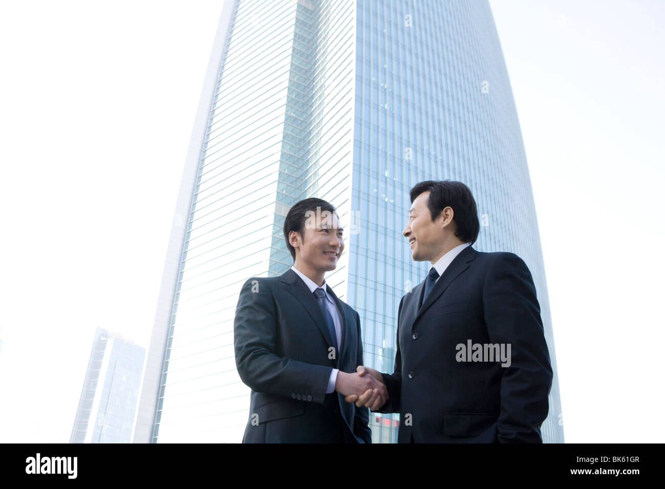Businessmen shaking hands in front of tall building Stock Photo - Alamy