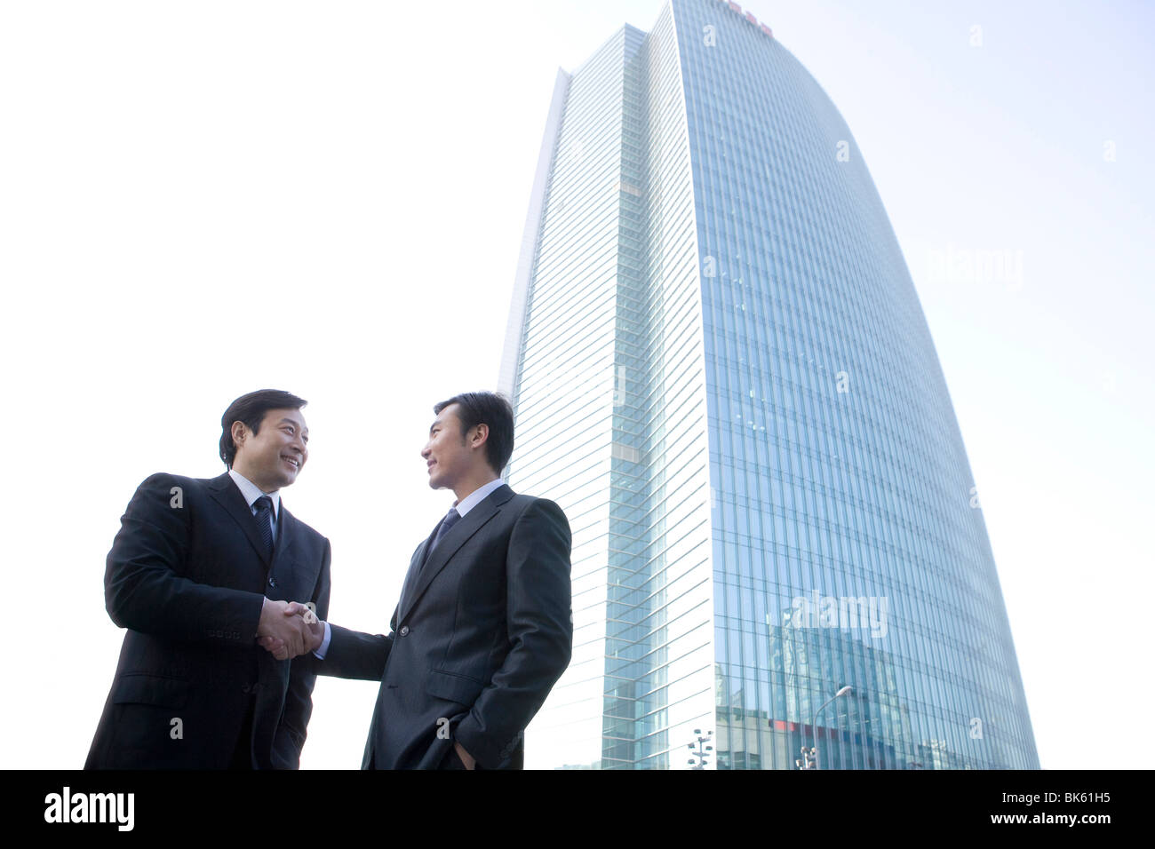 Businessmen shaking hands in front of tall building Stock Photo - Alamy