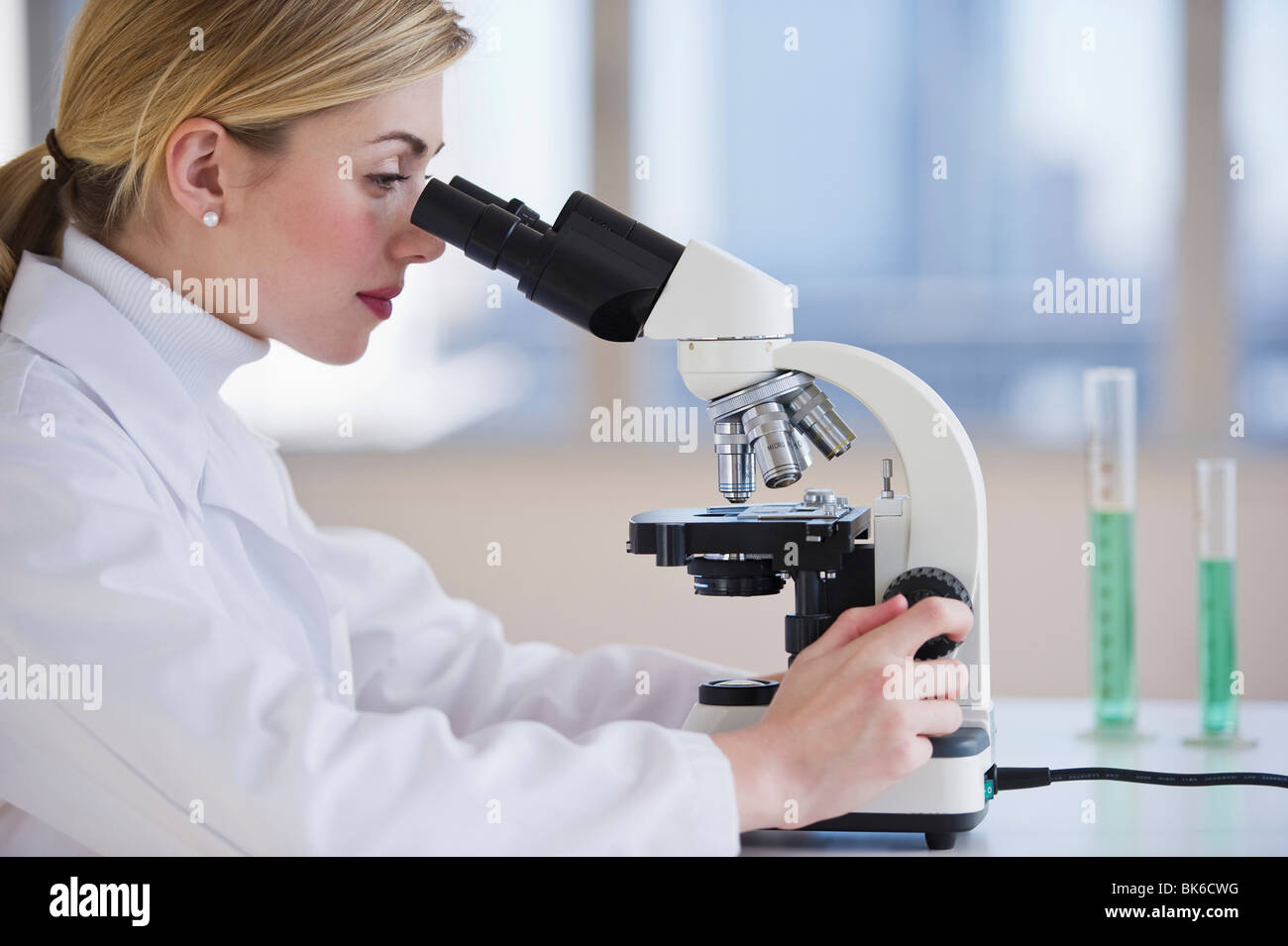 female scientist looking through microscope with test tubes in the ...