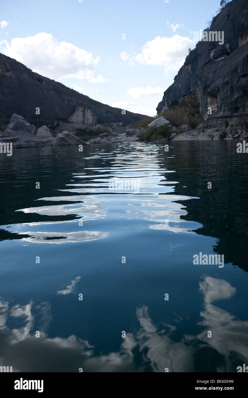 Rocky cliffs, blue sky and clouds reflect into the Pecos River arm of ...