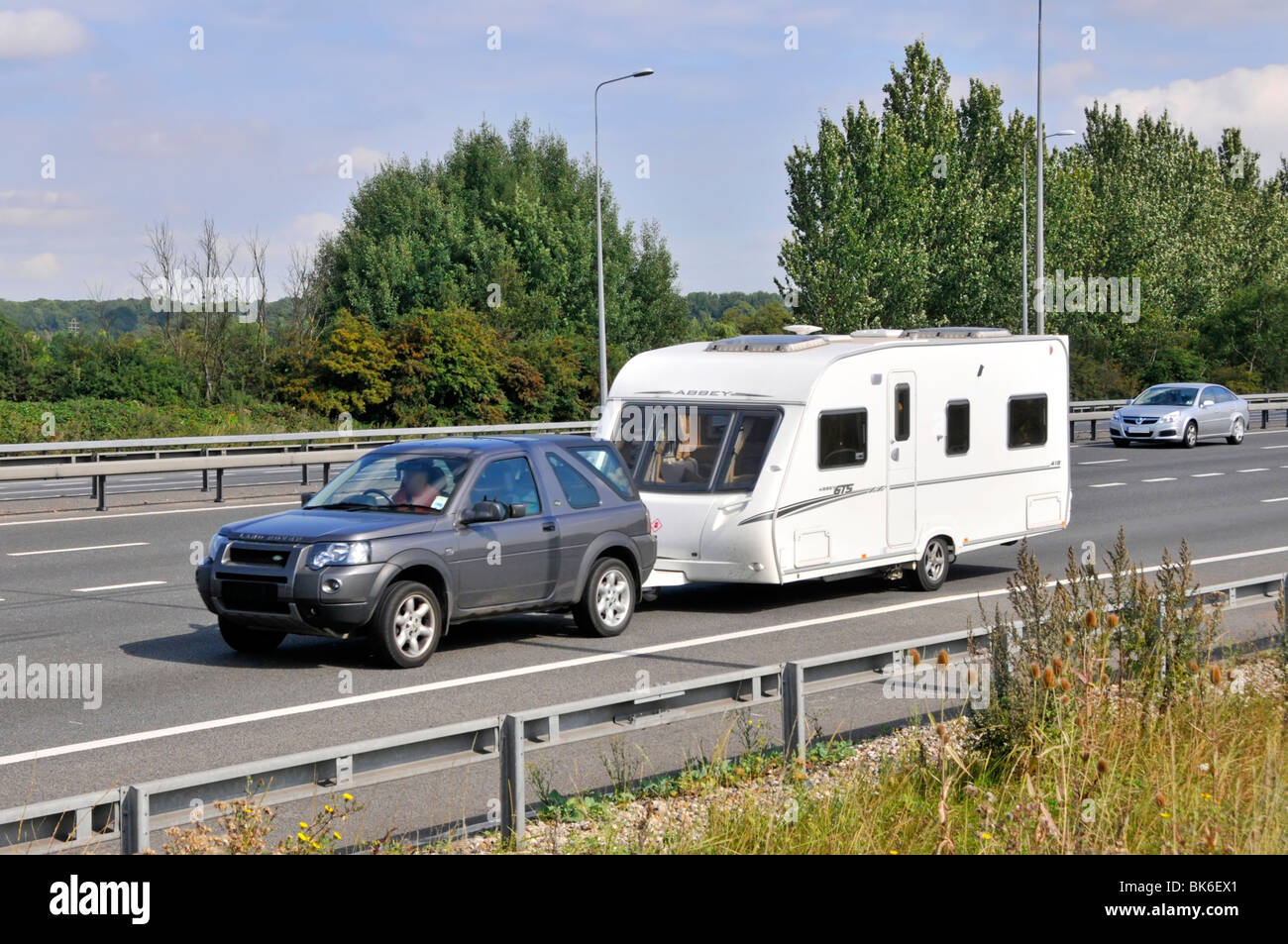 Land Rover car towing white caravan side front view driving along rural ...