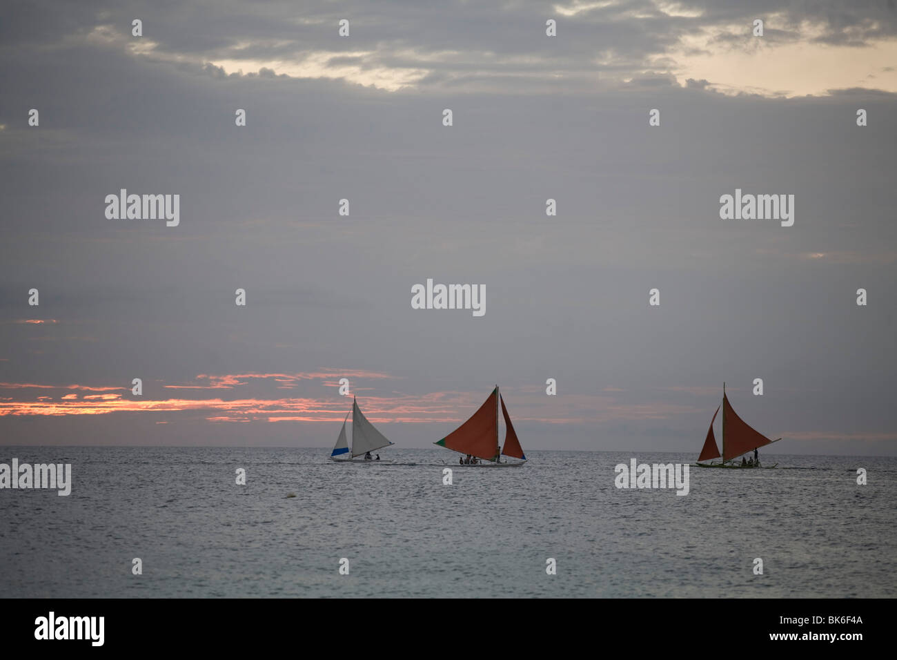 Three distant sailboats at sunset Stock Photo - Alamy