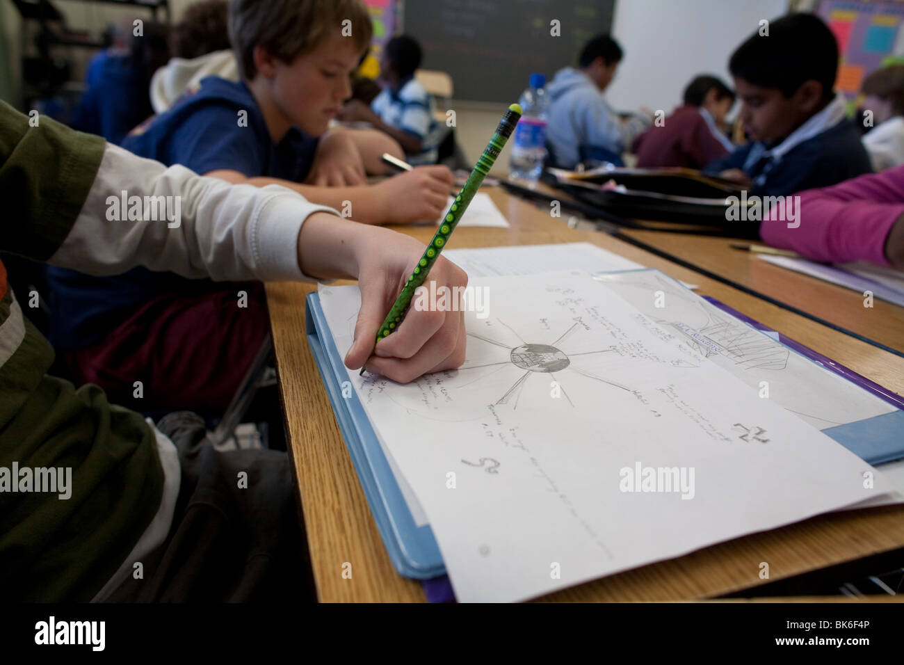 Left handed student draws on white paper with green pencil in classroom ...