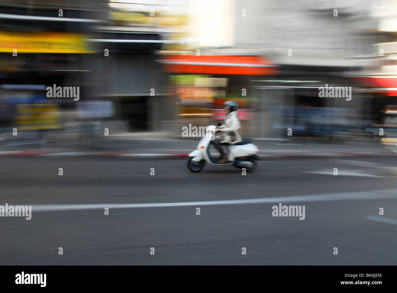 Urban scooter (moped) rider zooms past camera on a city street with ...