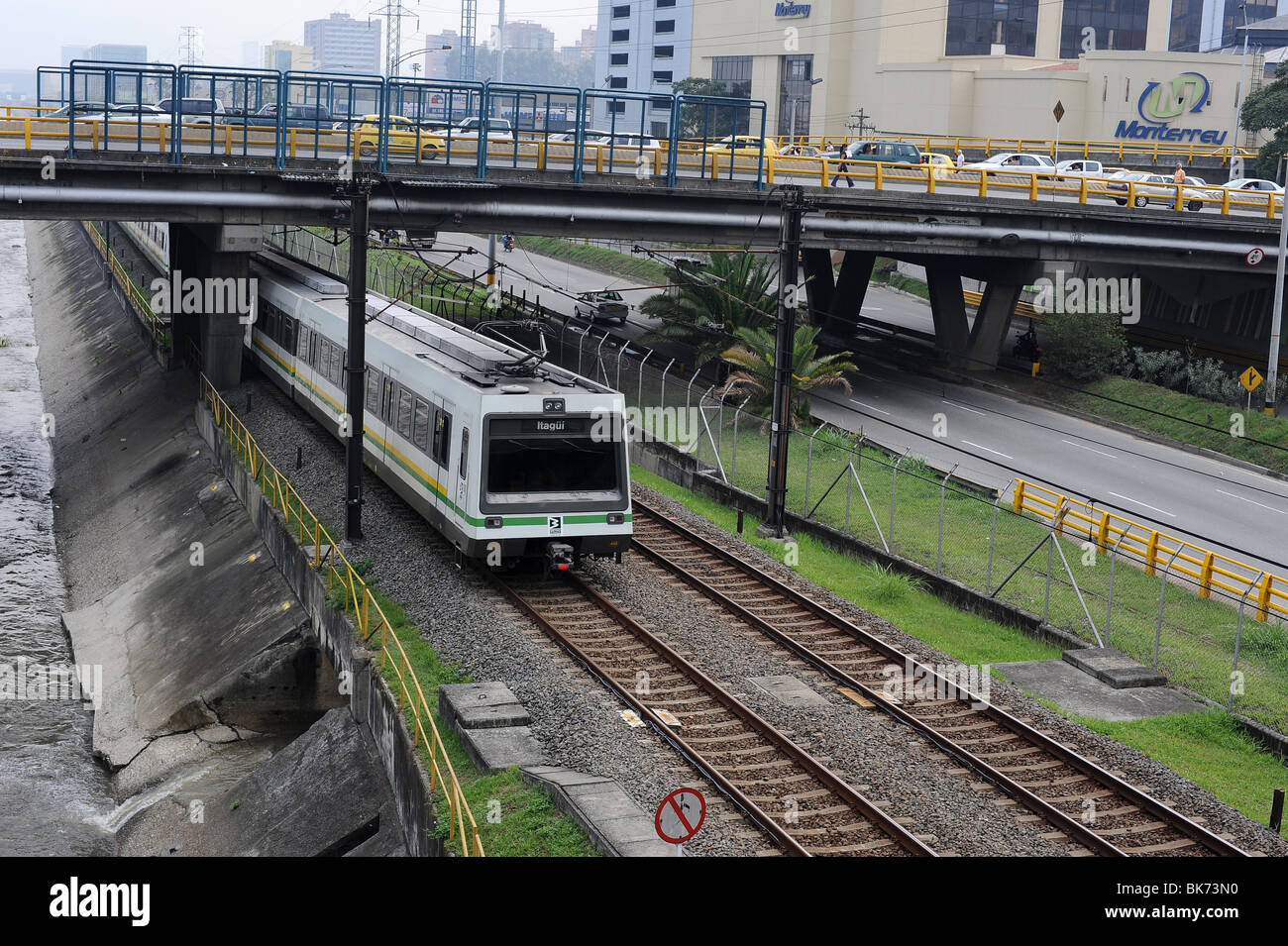 Overground metro traveling under bridge with a road one side and a ...