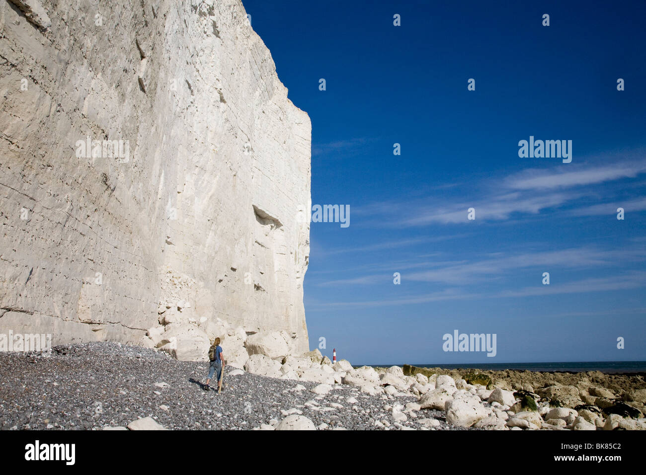 A man walks along the base of the cliff, on the beach, towards Beachy ...