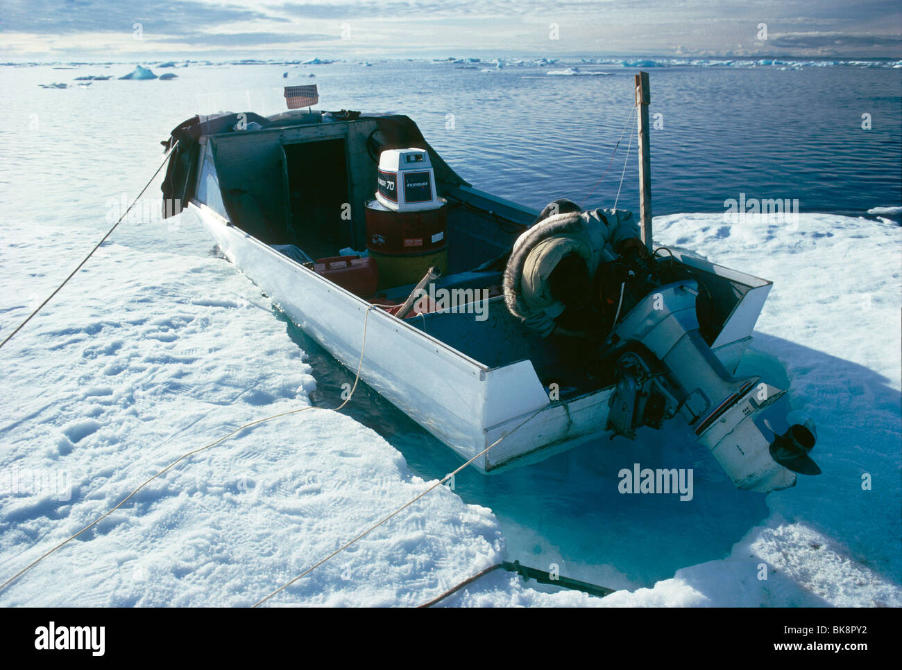 Native Inuit hunter repairs outboard motor on an Inuit Freighter Canoe ...