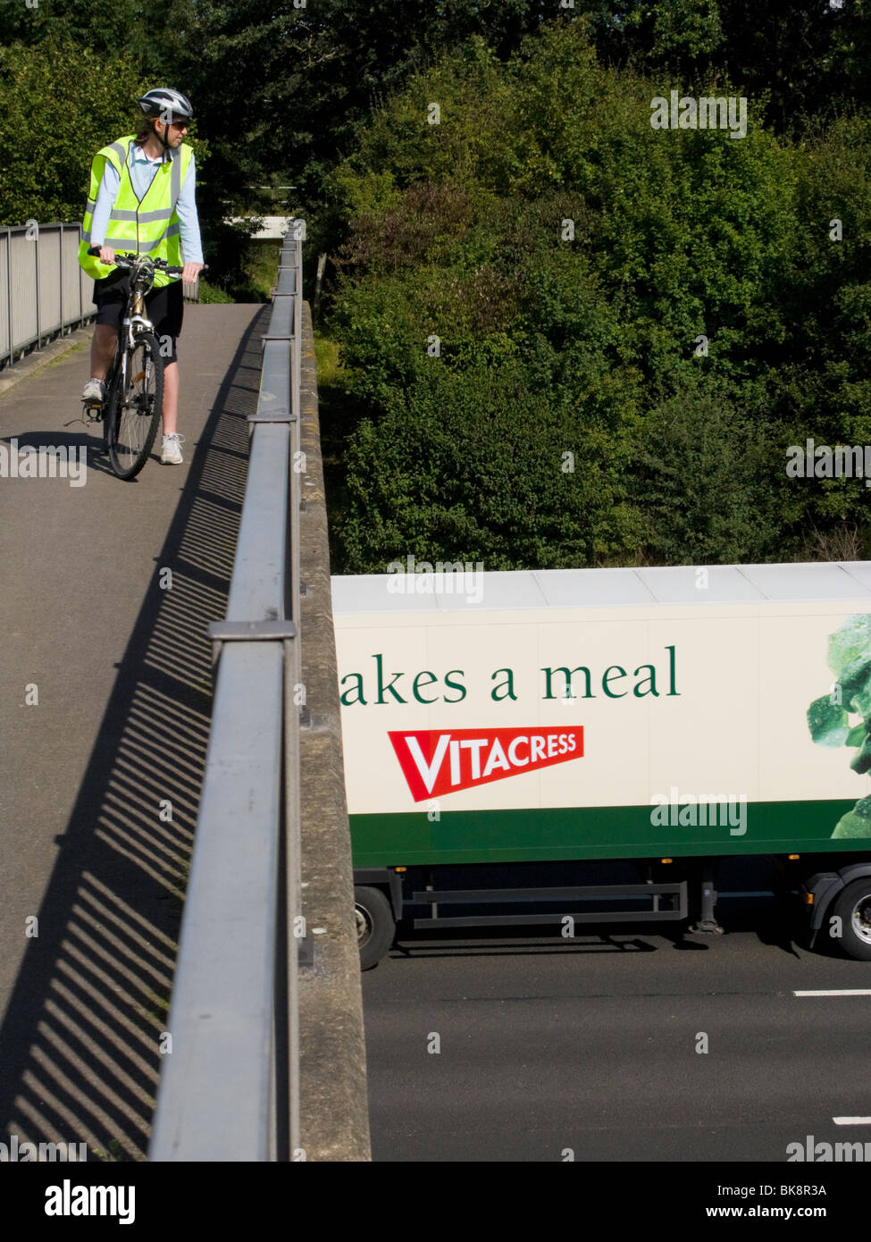 Cyclist on a pedestrian / cycle / footbridge looks down on lorry ...