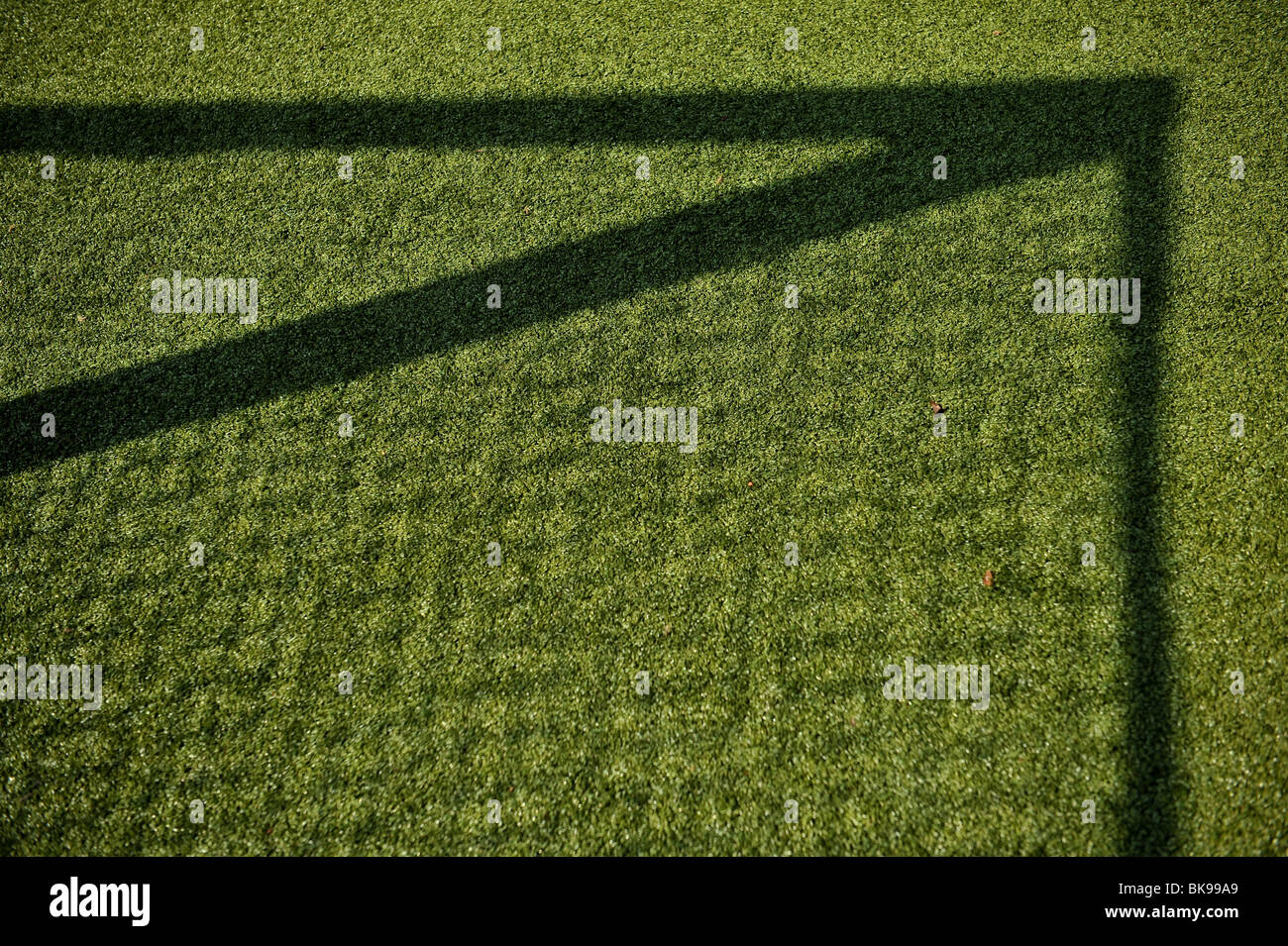 A shadow from a hockey goal net shines onto a green outdoor astro turf ...