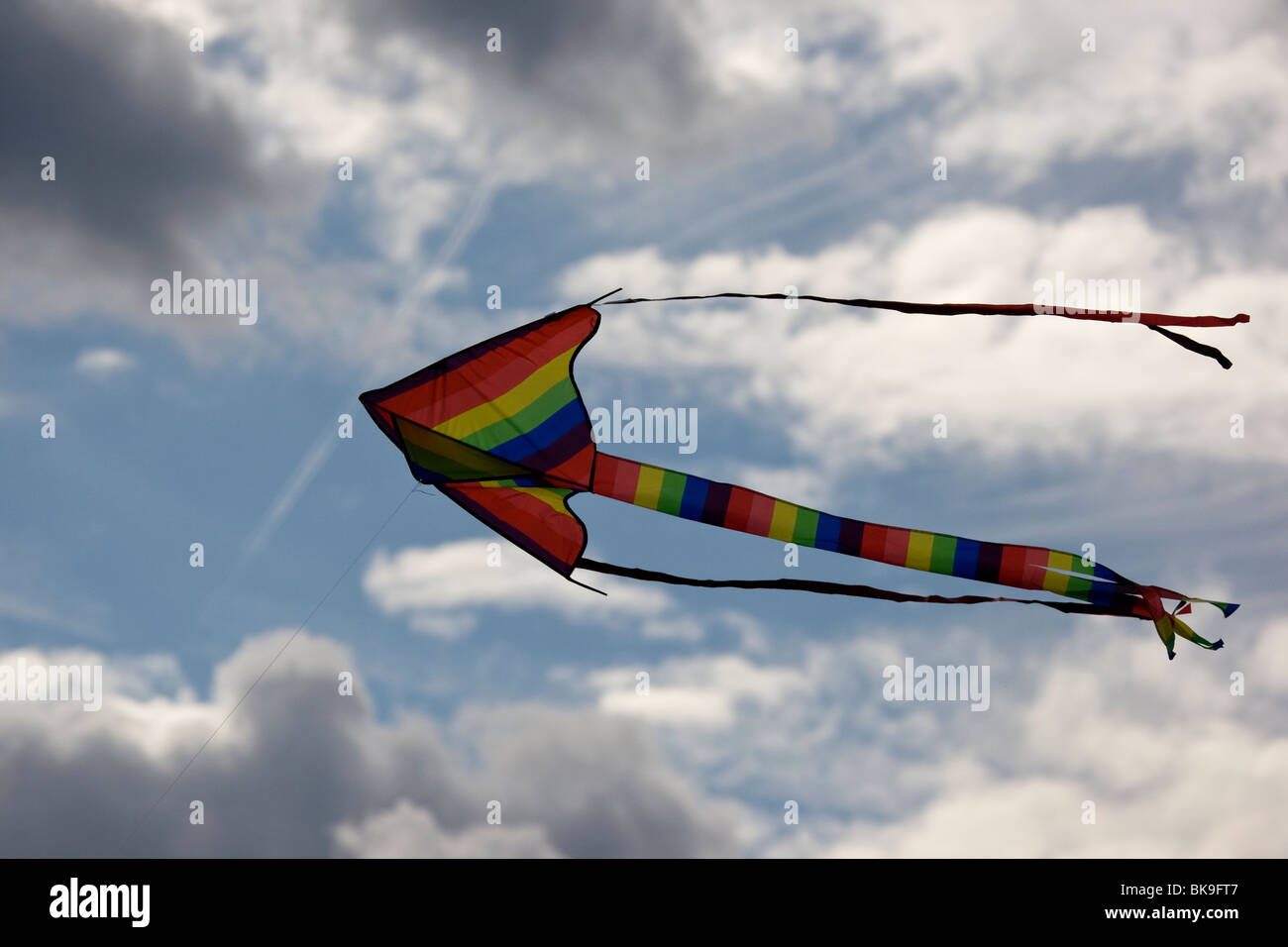 Colourful kite flying in a bright blue sky with dominant fluffy white ...