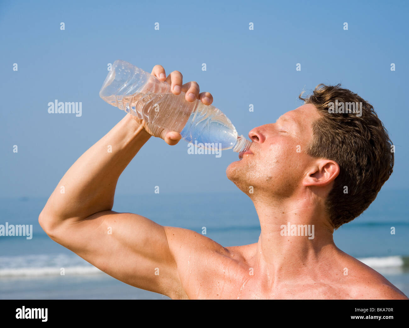 A man drinking bottled water on a beach Stock Photo - Alamy