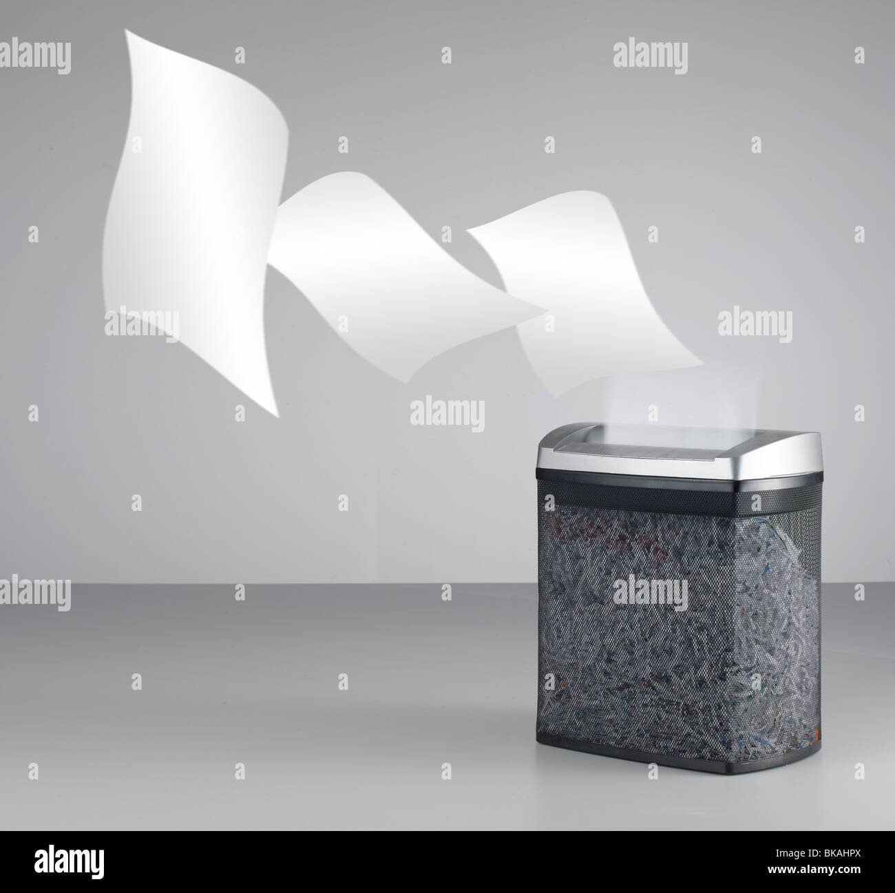 Paper shredder surrounded by flying paper sheets on a grey background ...