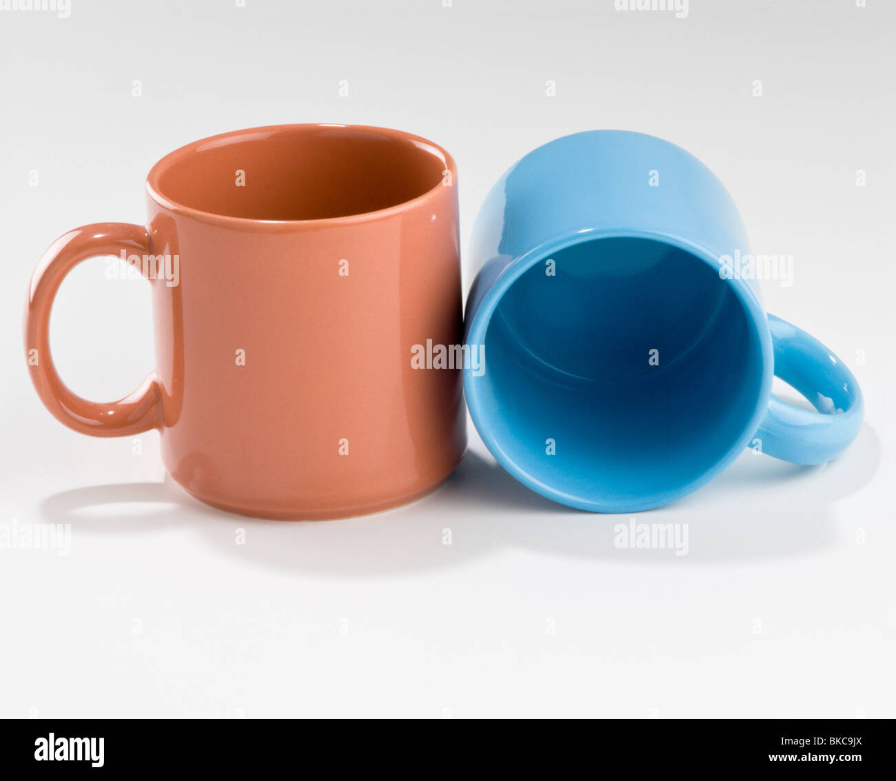 Two pastel ceramic coffee mugs with one tipped over Stock Photo - Alamy