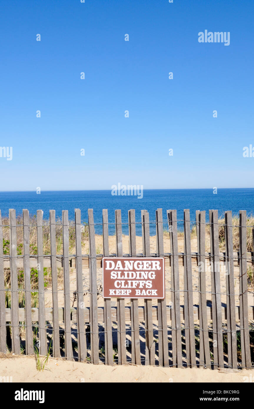Beach fence and warning sign at edge of cliff to ocean on Cape Cod ...
