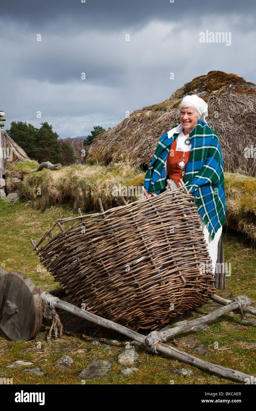 Woman (MR in Traditional dress, woven basket & thatched Scottish croft ...