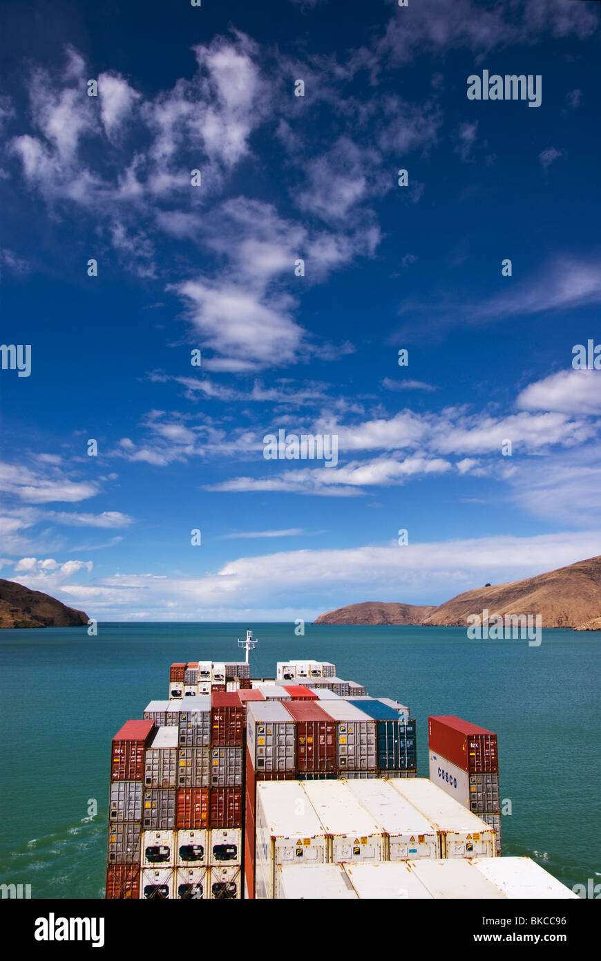 View of deck stacked with containers as ship sails down the harbour ...