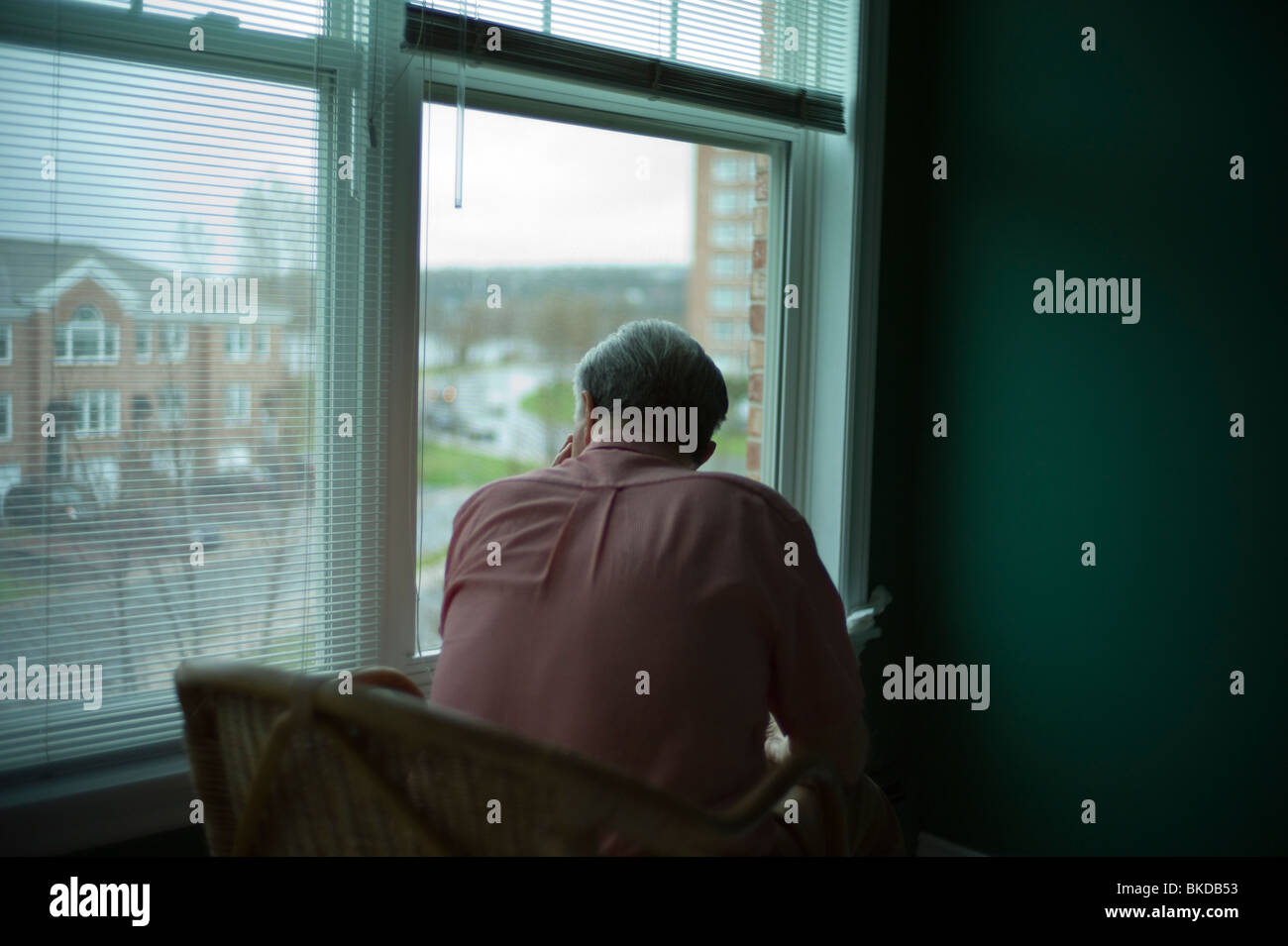 Old man sits in chair looking out bedroom window Stock Photo - Alamy