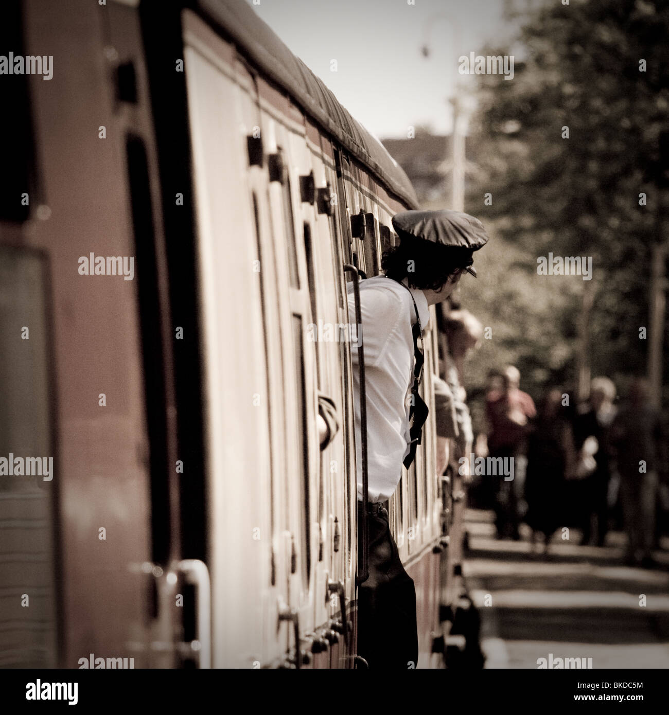 A train conductor leans out of the door as a steam train approaches a ...