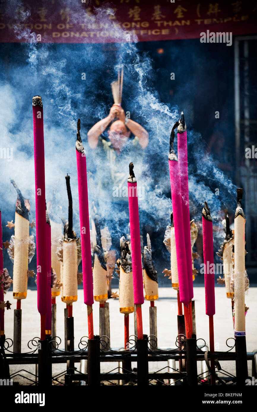 a Chinese man at worship with burning incense in the foreground at ...
