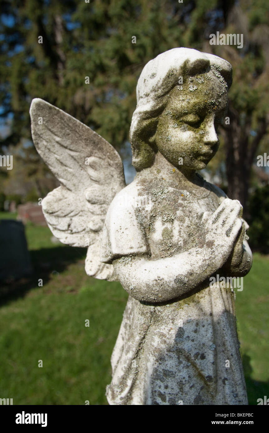 A statue of an angelic child is frozen in time with its' hands clasped ...
