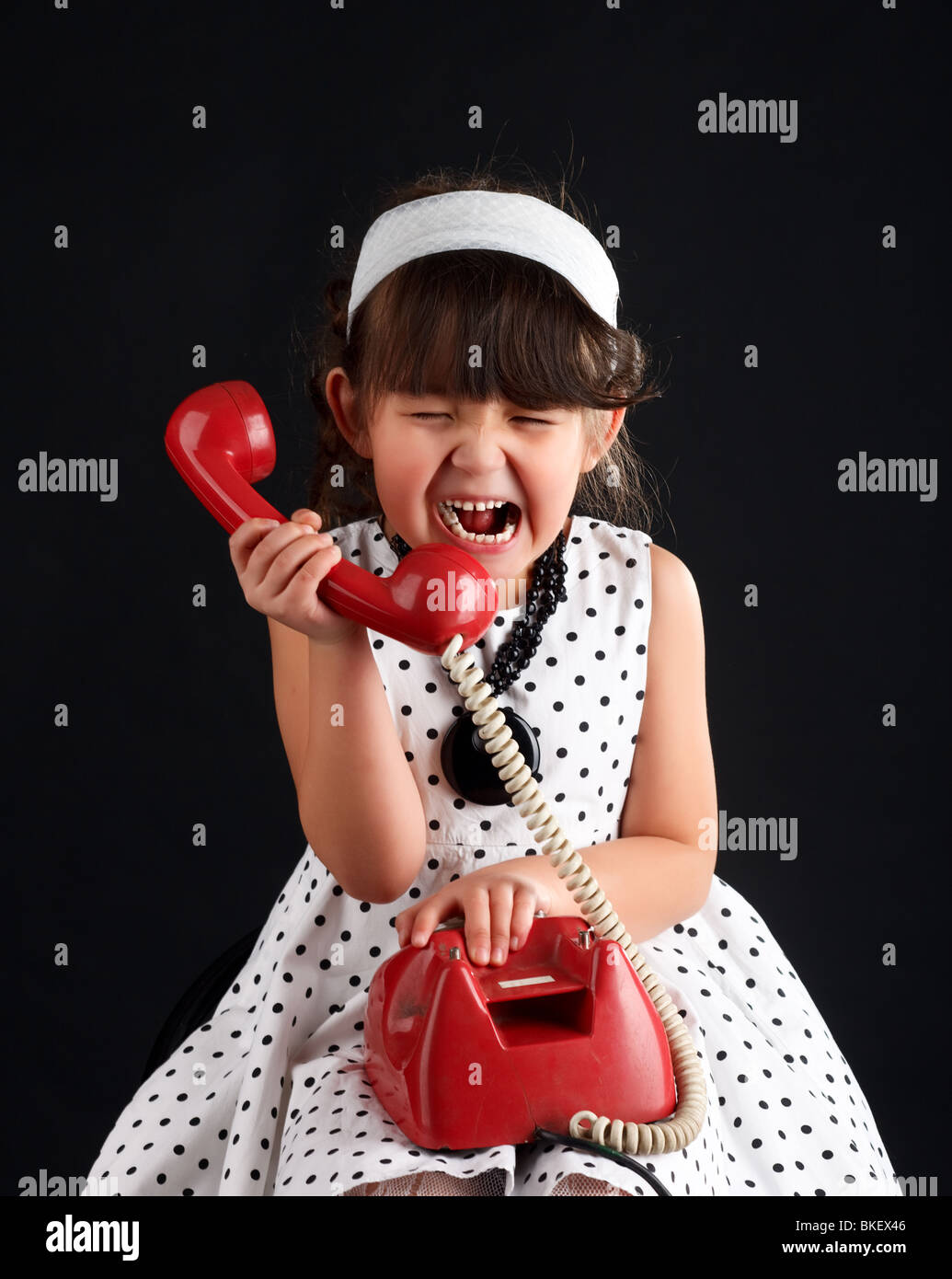 Little fashion model with red phone posing in studio Stock Photo - Alamy
