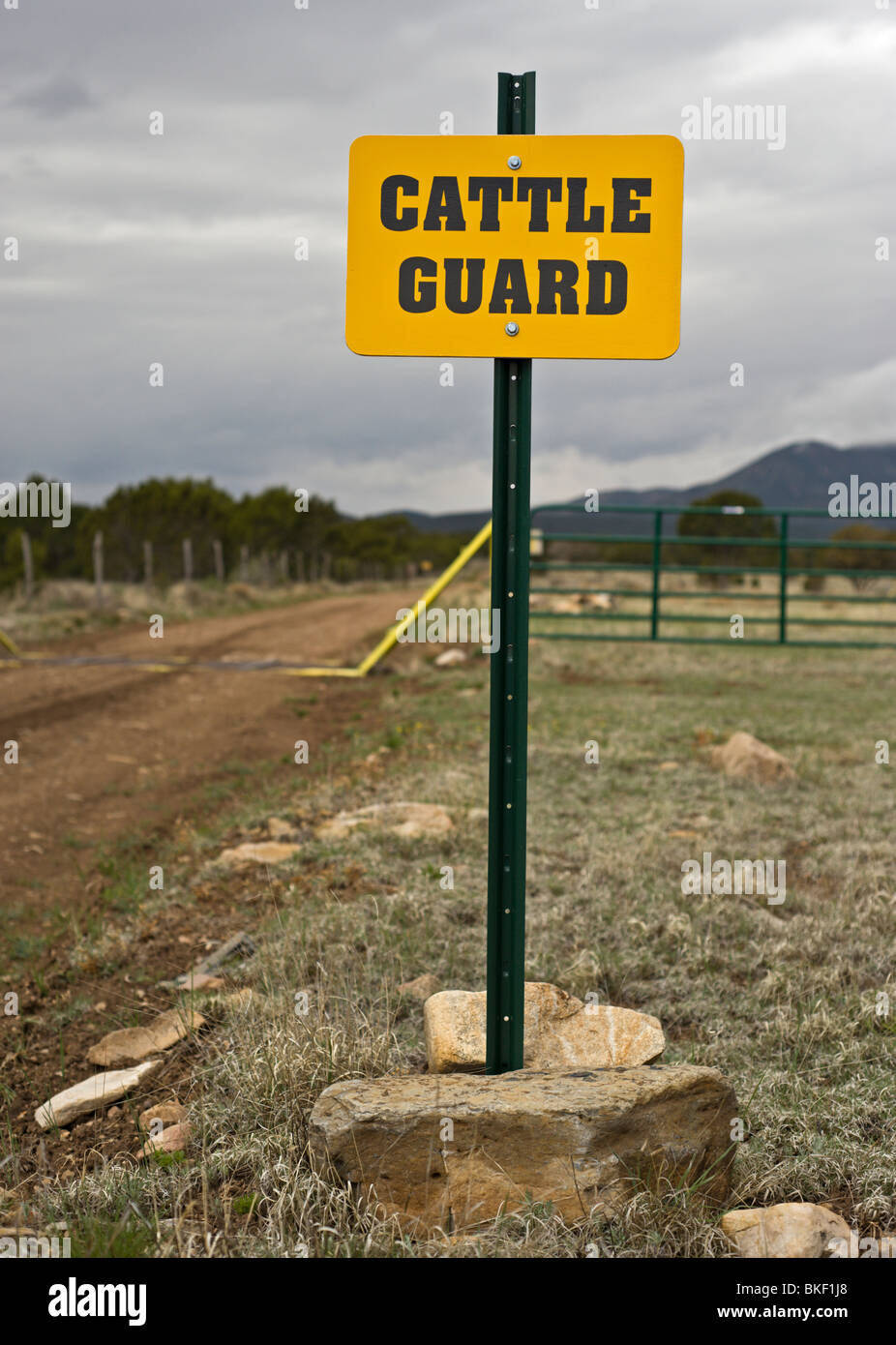 Underneath a stormy sky stands a cattle guard sign, near the ghost town ...