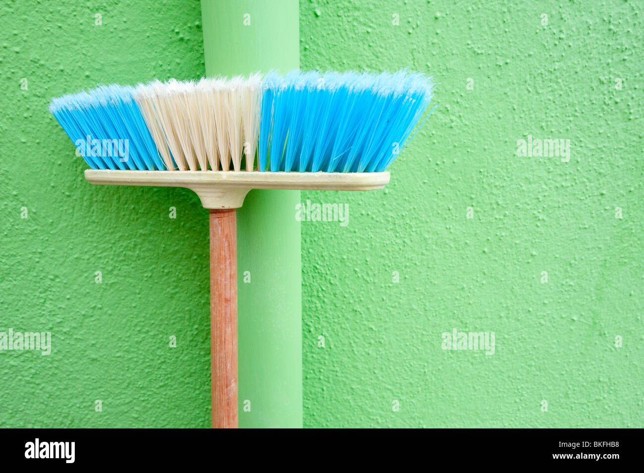 Household broom leaning against lime green wall of house in Burano ...