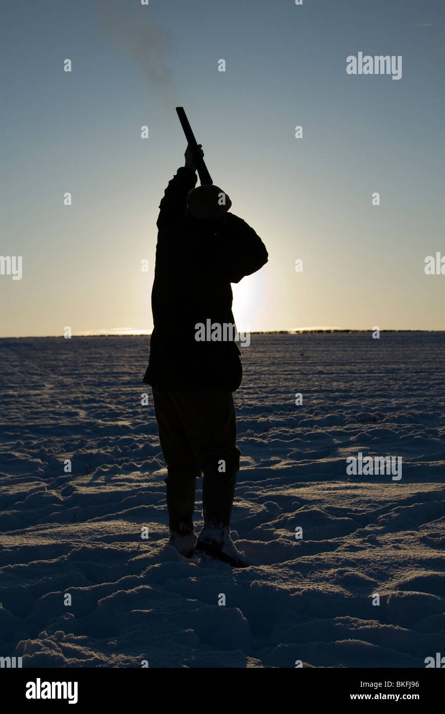 A silhouette of man in sunlight, firing his gun in a field in the snow ...
