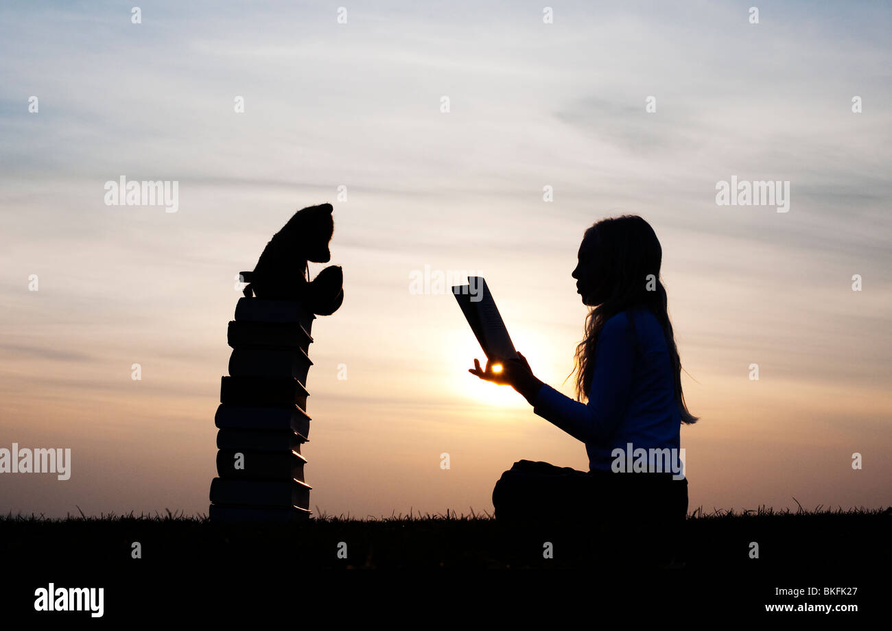 Young Girl sitting down reading a book opposite a teddy bear sitting on ...