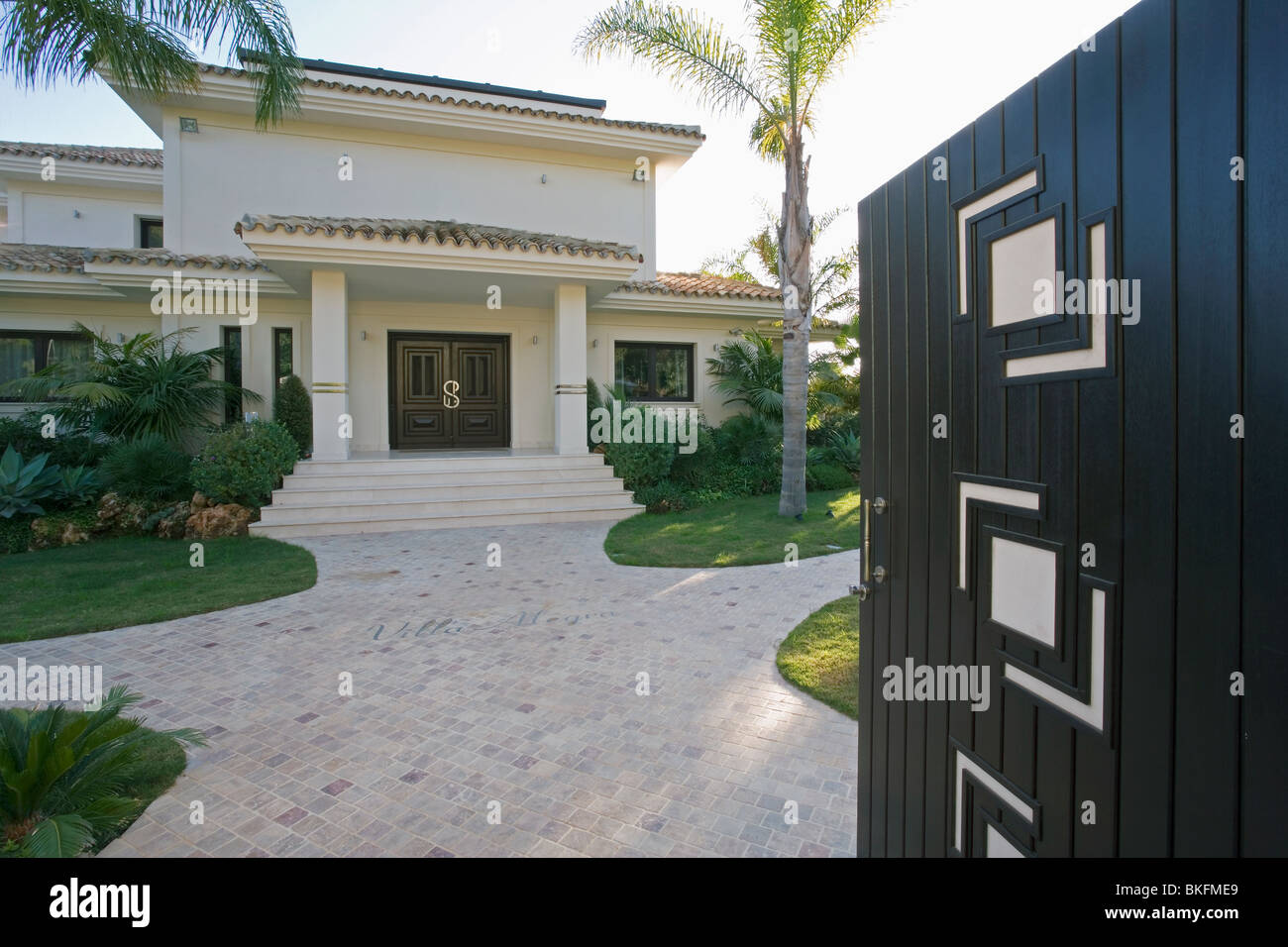 Gates open to paved area in front of large white Spanish villa with ...