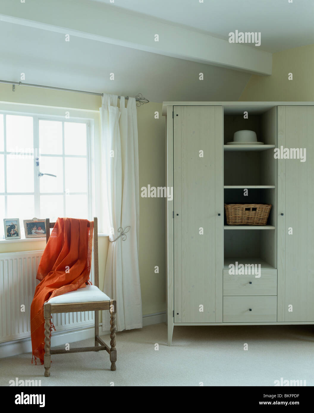 Red throw on chair in front of window in white bedroom with white ...