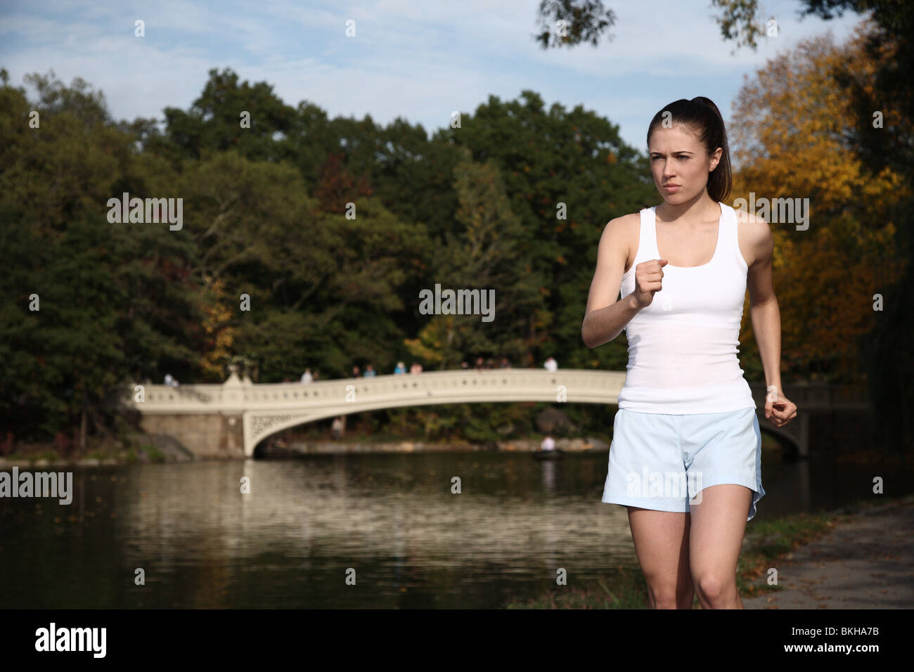 Woman running by river with bridge in background in park Stock Photo ...