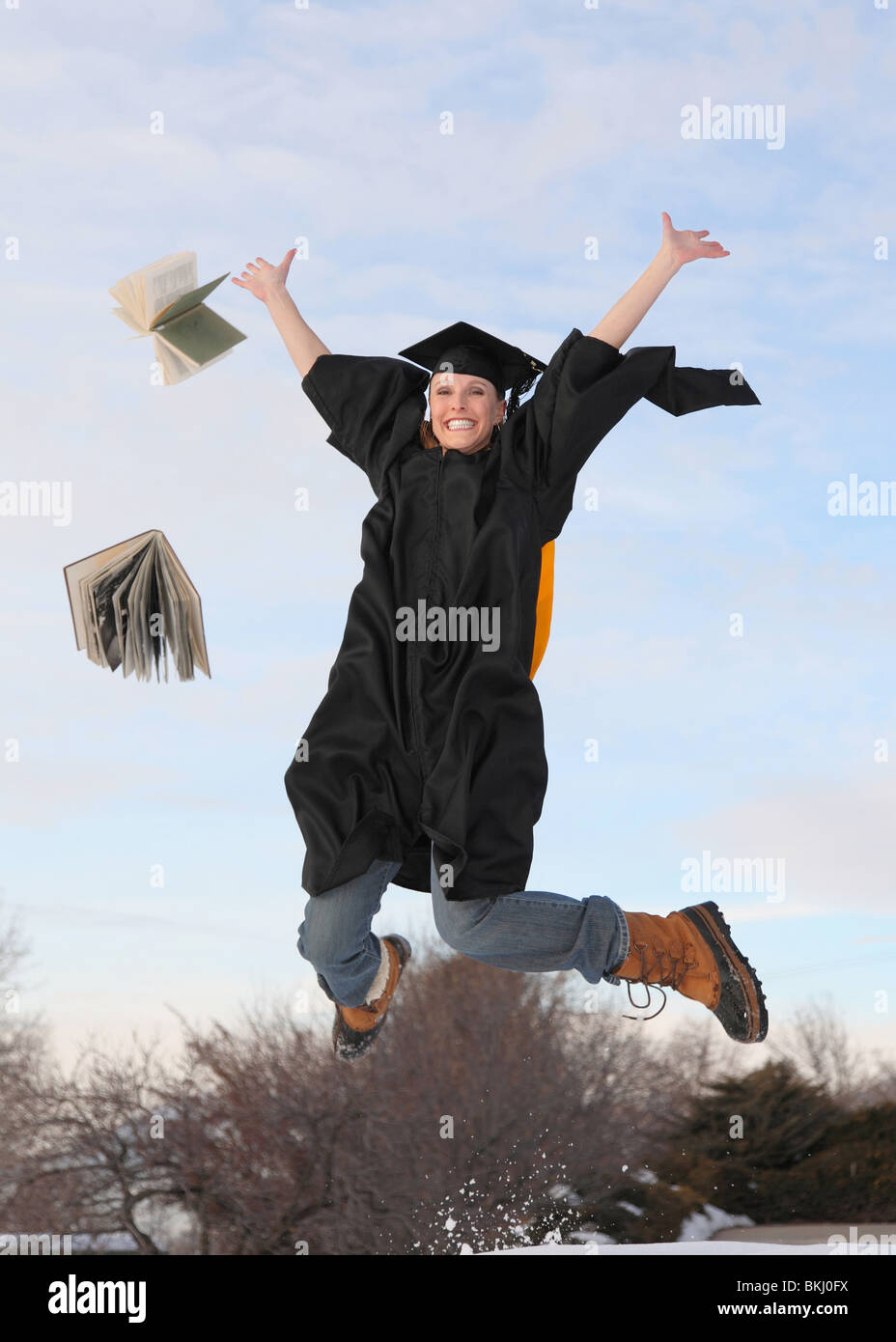 excited college graduate leaping in air and throwing books upwards ...