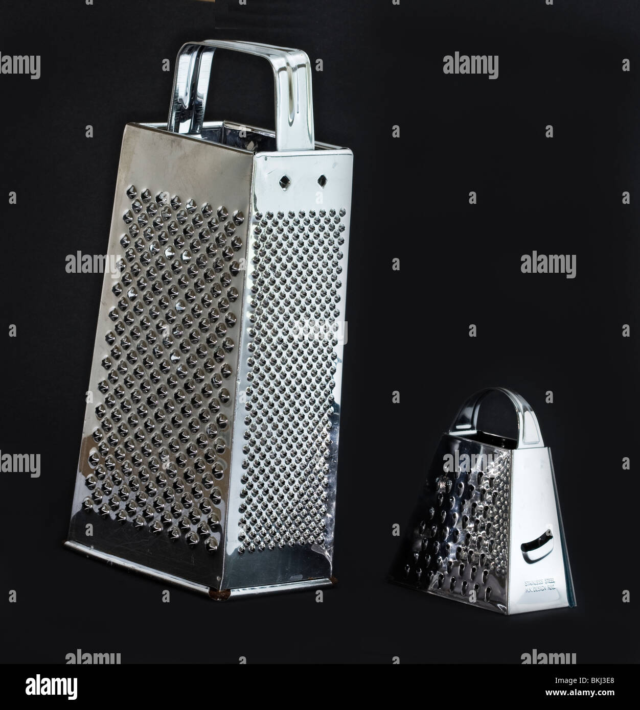 Large and small stainless steel cheese graters on a plain black ...