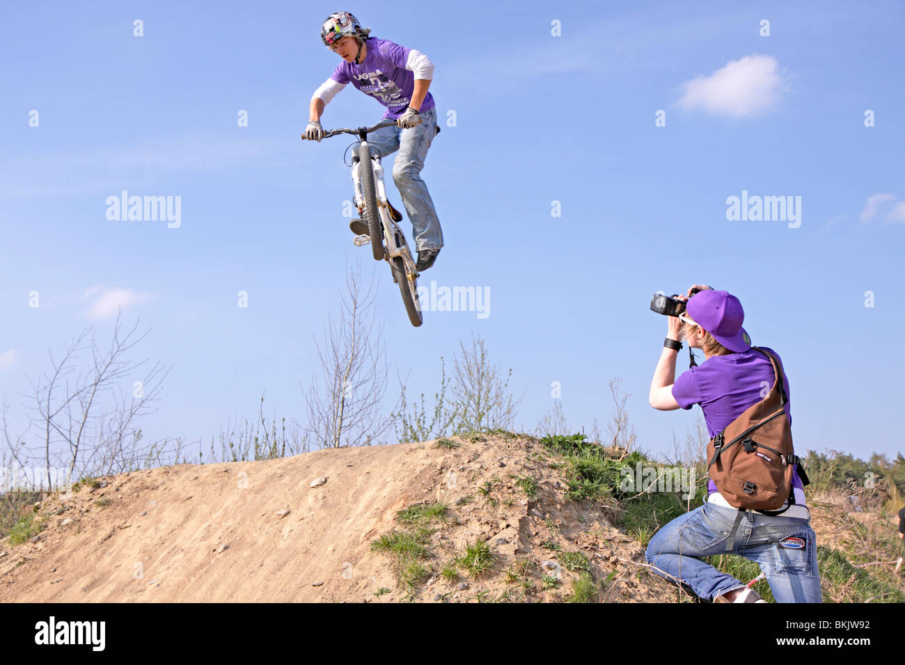 teenage boy jumping with his bike, his friend taking of photo of him ...
