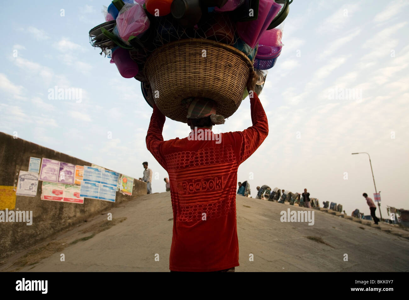 A man carrying a bowl of clothes on his head walks up a steep slope on ...