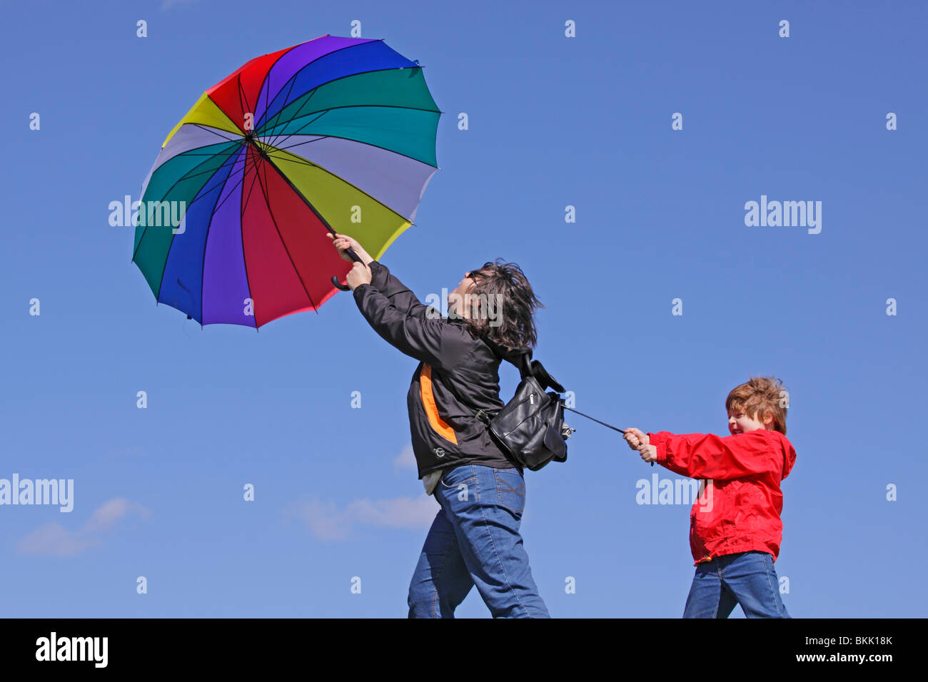young boy holding on to his mother who is being blown away by the wind ...