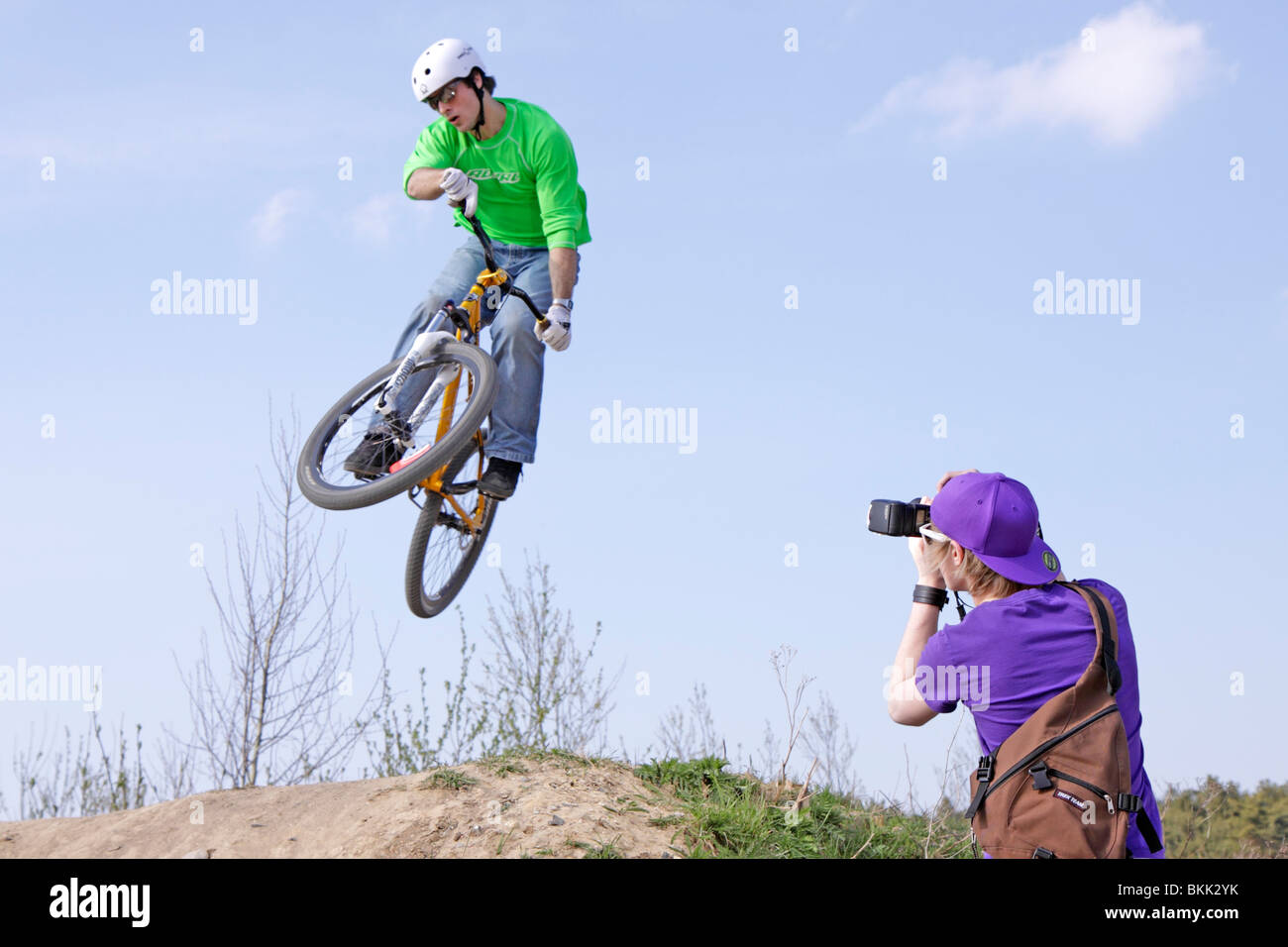 young man jumping with his bike, his friend taking of photo of him ...